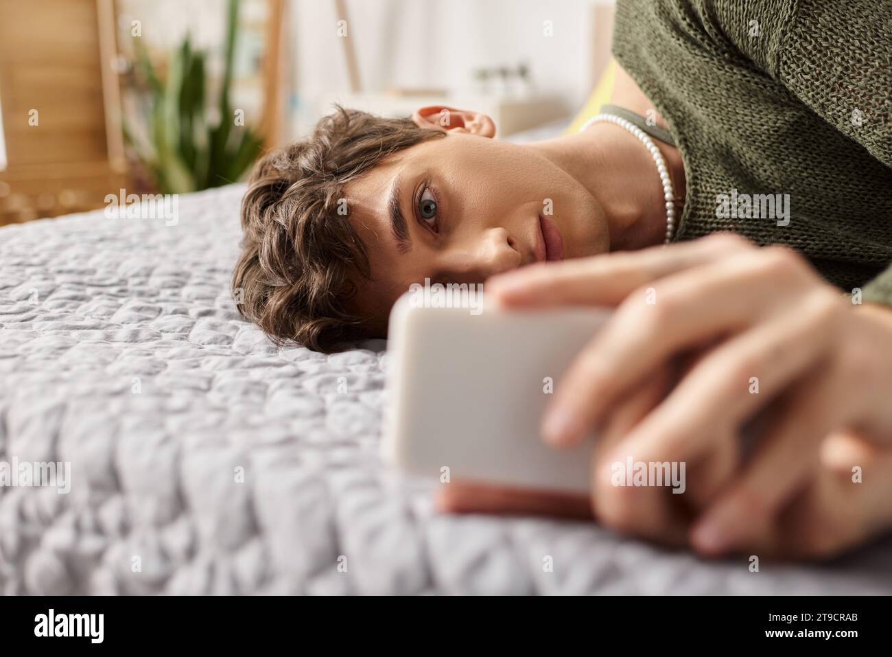 transgender blogger with curly hair using smartphone and lying on bed ...