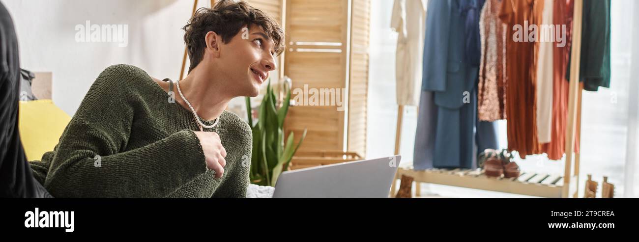 happy and curly transgender blogger using laptop in bedroom at home ...