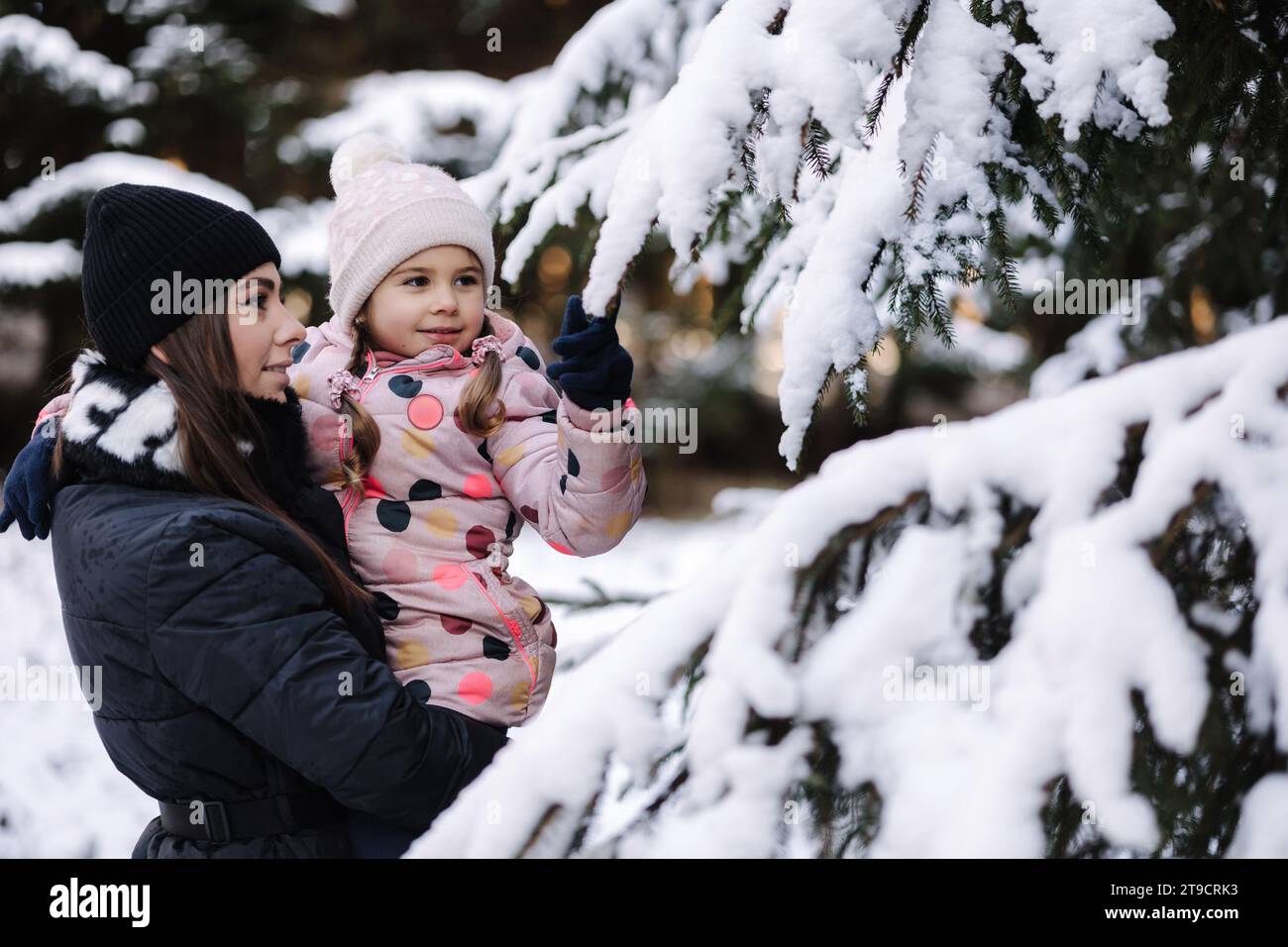Happy mom and daughter shake off the snow from a Christmas tree branch ...