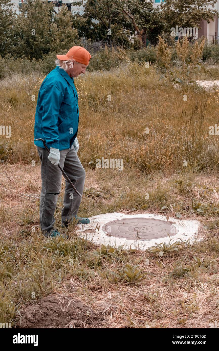 A working man with a crowbar stands near a well. Inspection of wells ...