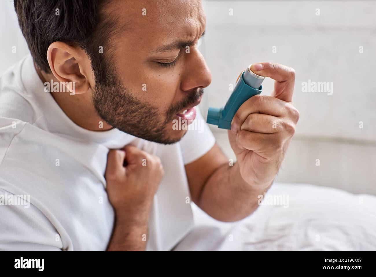 young indian patient using asthma inhaler while lying in bed in his ...