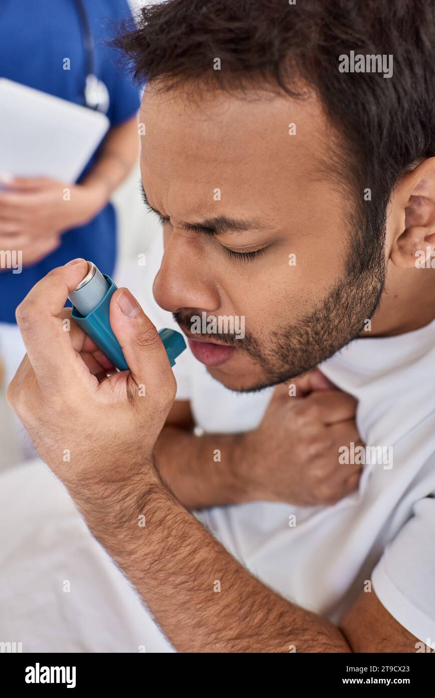 cropped view of indian man using asthma inhaler with blurred nurse on ...