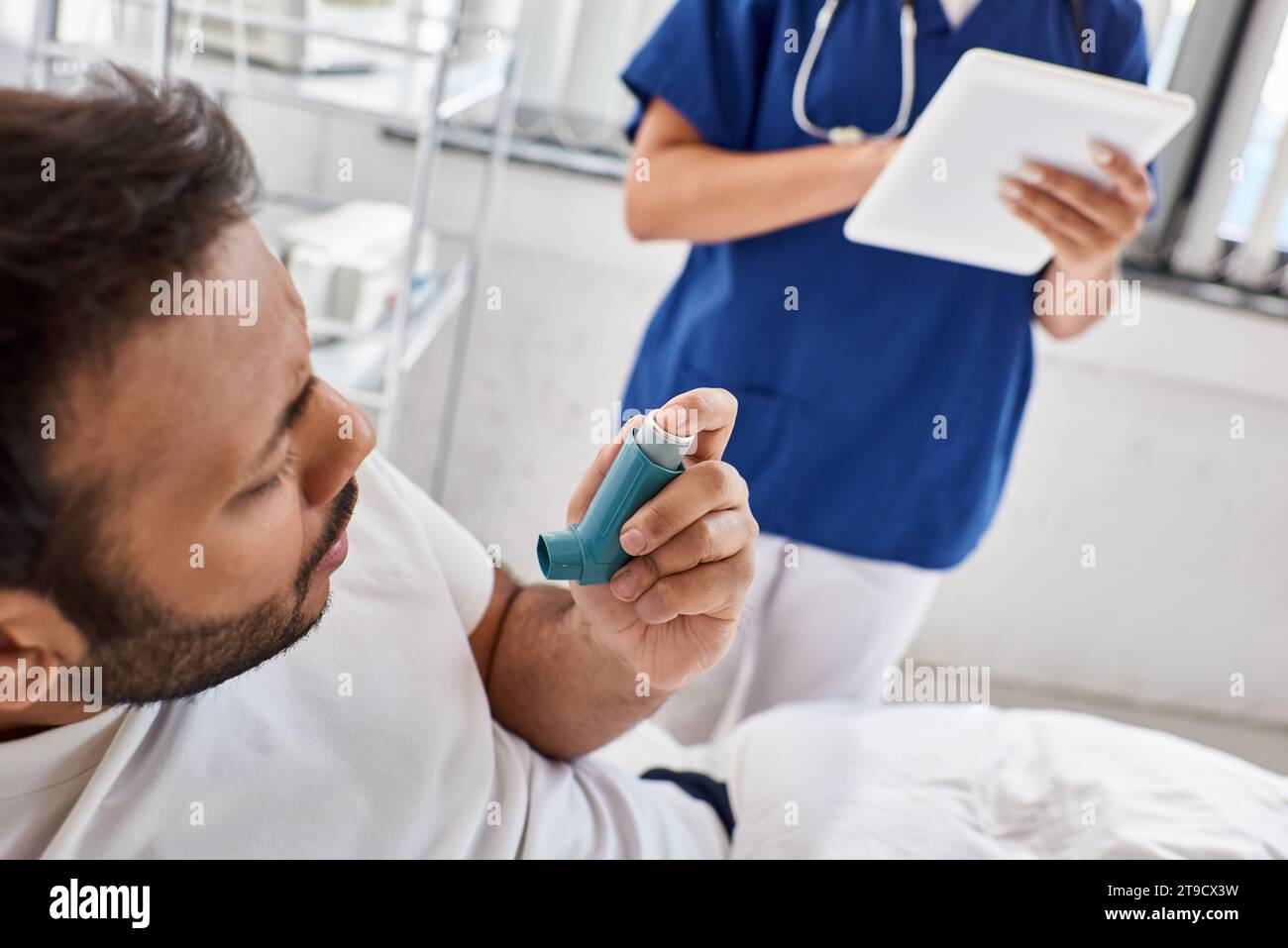 cropped view of indian man using asthma inhaler with blurred nurse on ...