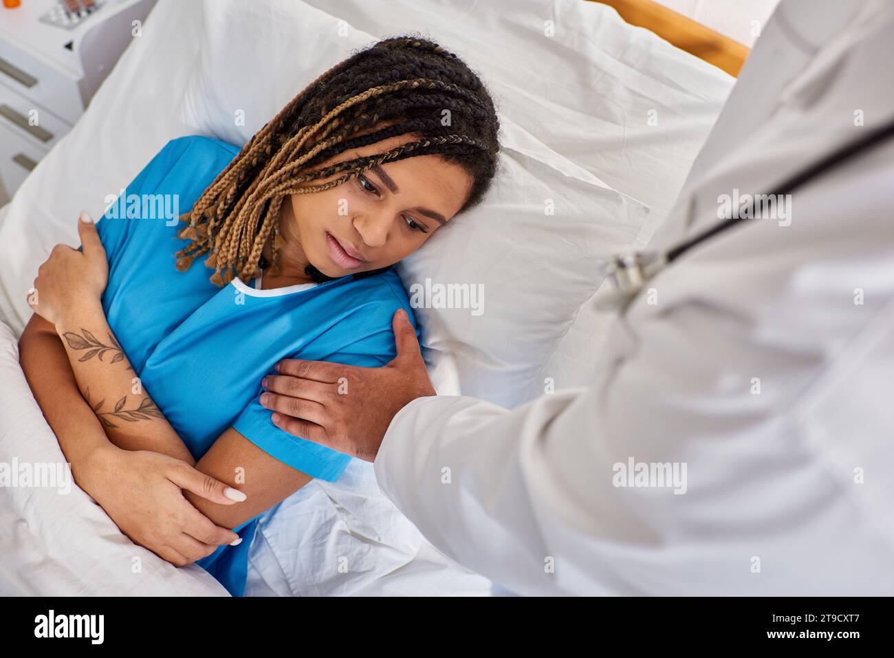 cropped view of indian doctor comforting his ill sad african american ...