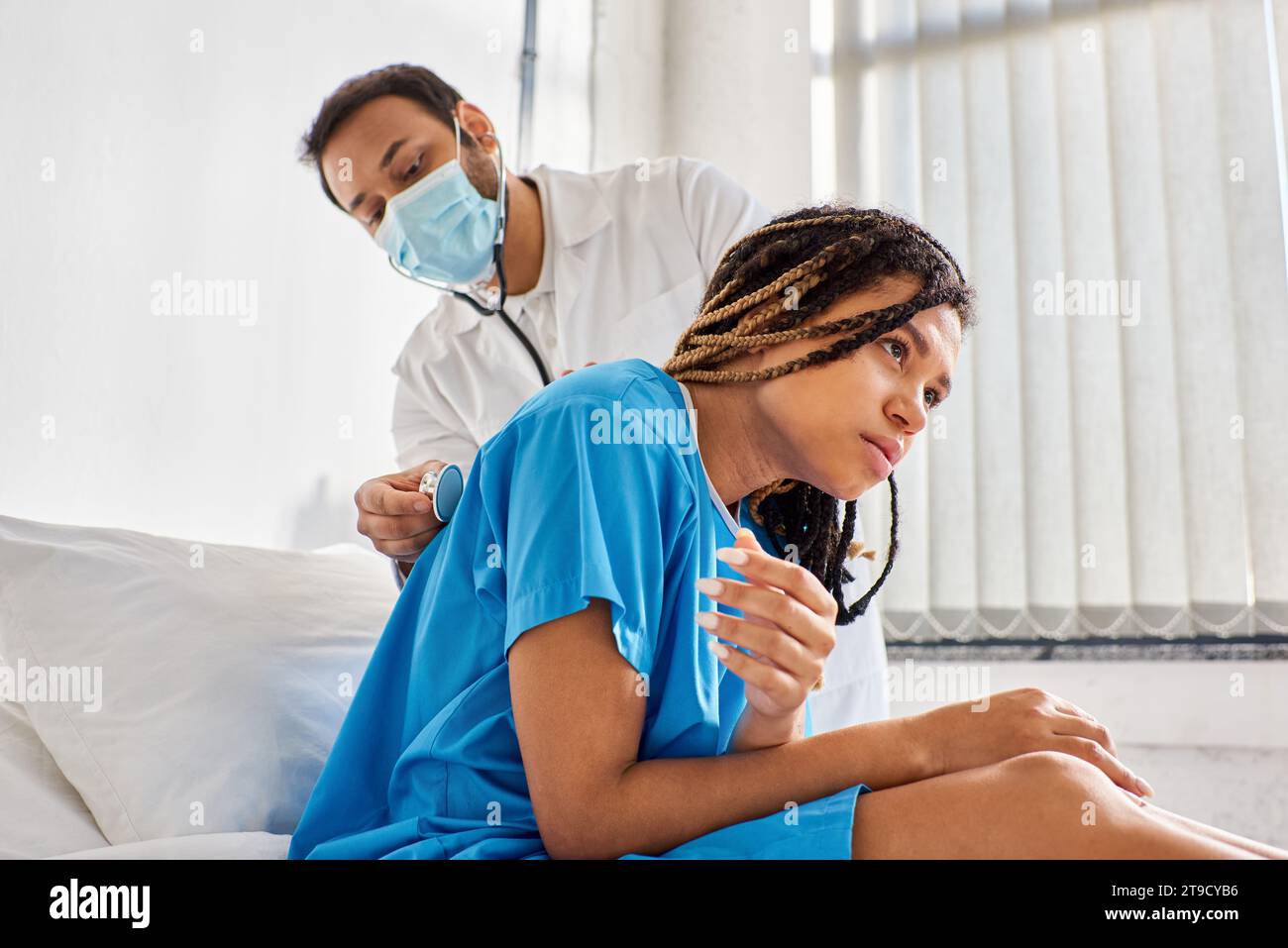 young indian doctor examining breath of ill african american patient ...