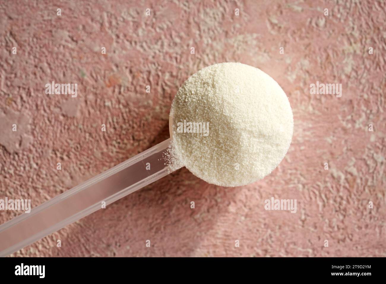 White collagen powder in a plastic scoop on pink background, top view ...