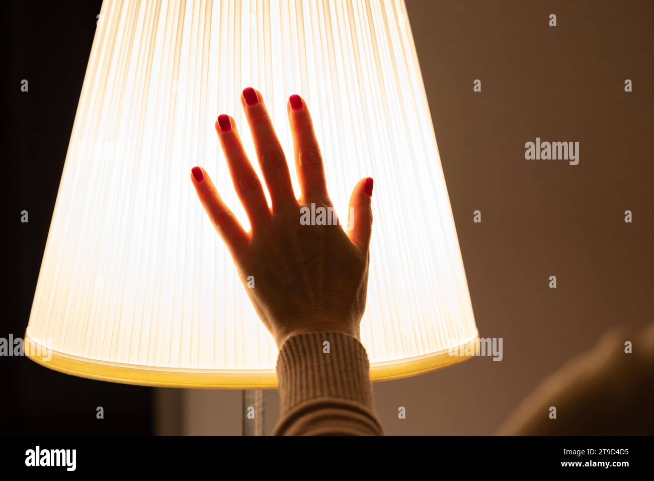 a woman's hand touches a floor lamp in a dark room. woman's hand on a ...