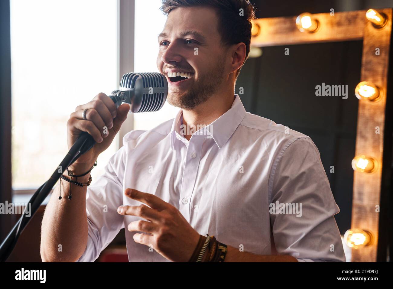 Young smiling bearded man is singing into a microphone at home with ...