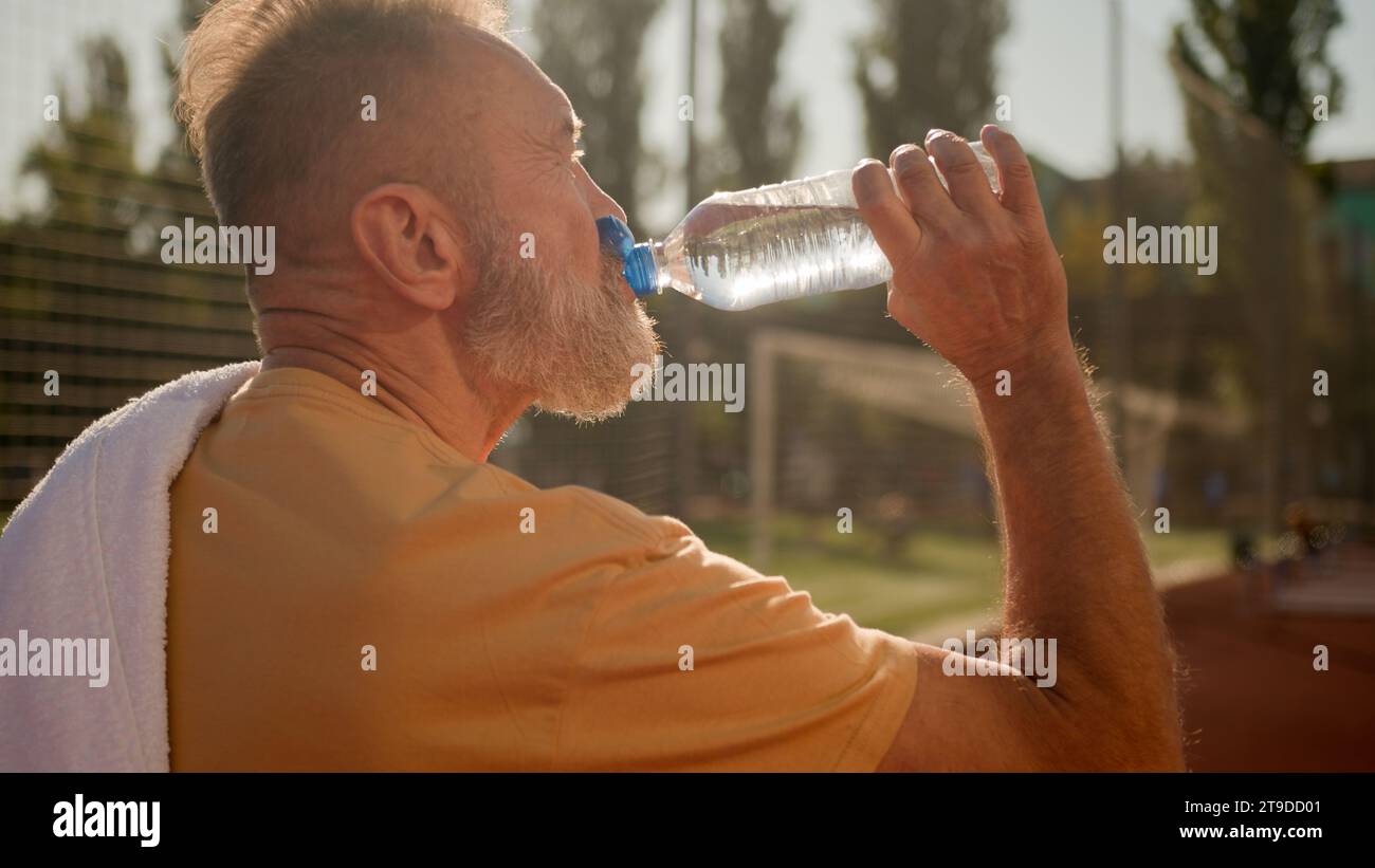 Back view old male sportsman athlete walking stadium outdoors drinking ...