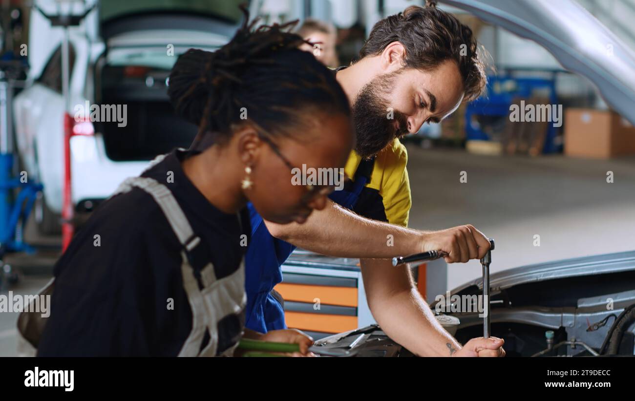Close up shot of coworking mechanics in car service using torque wrench ...
