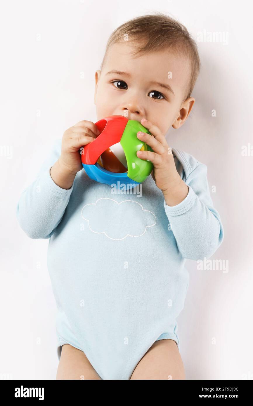 Adorable little boy in a romper is lying and playing with plastic toy ...