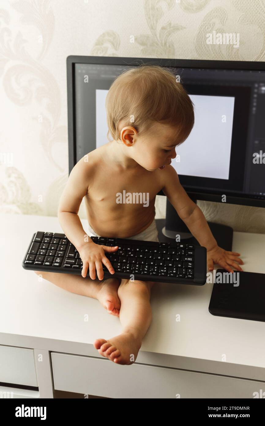 Little boy is sitting on a desk and playing with computer peripherals ...