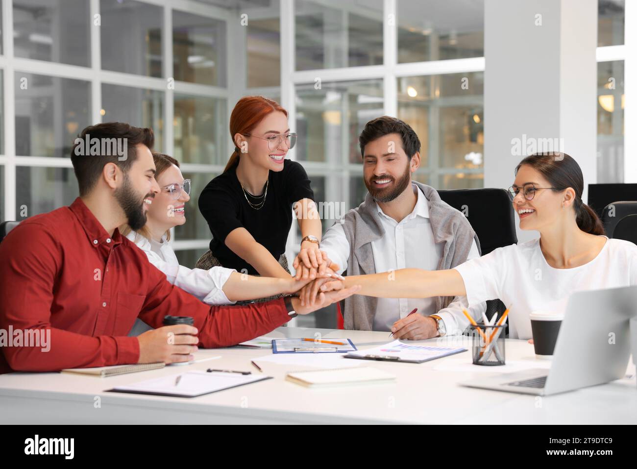 Team of employees joining hands in office Stock Photo - Alamy