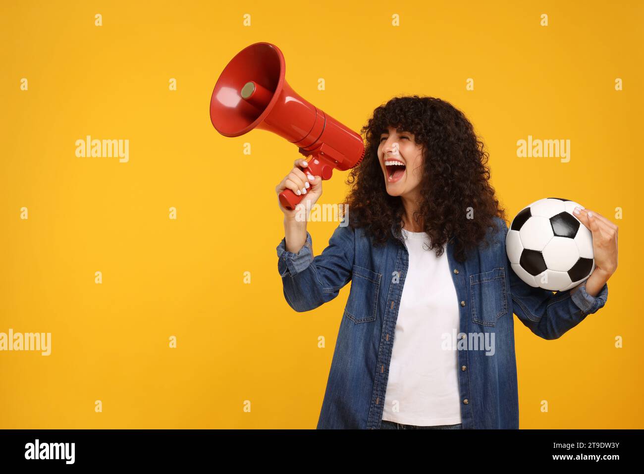Happy fan with soccer ball using megaphone on yellow background, space ...