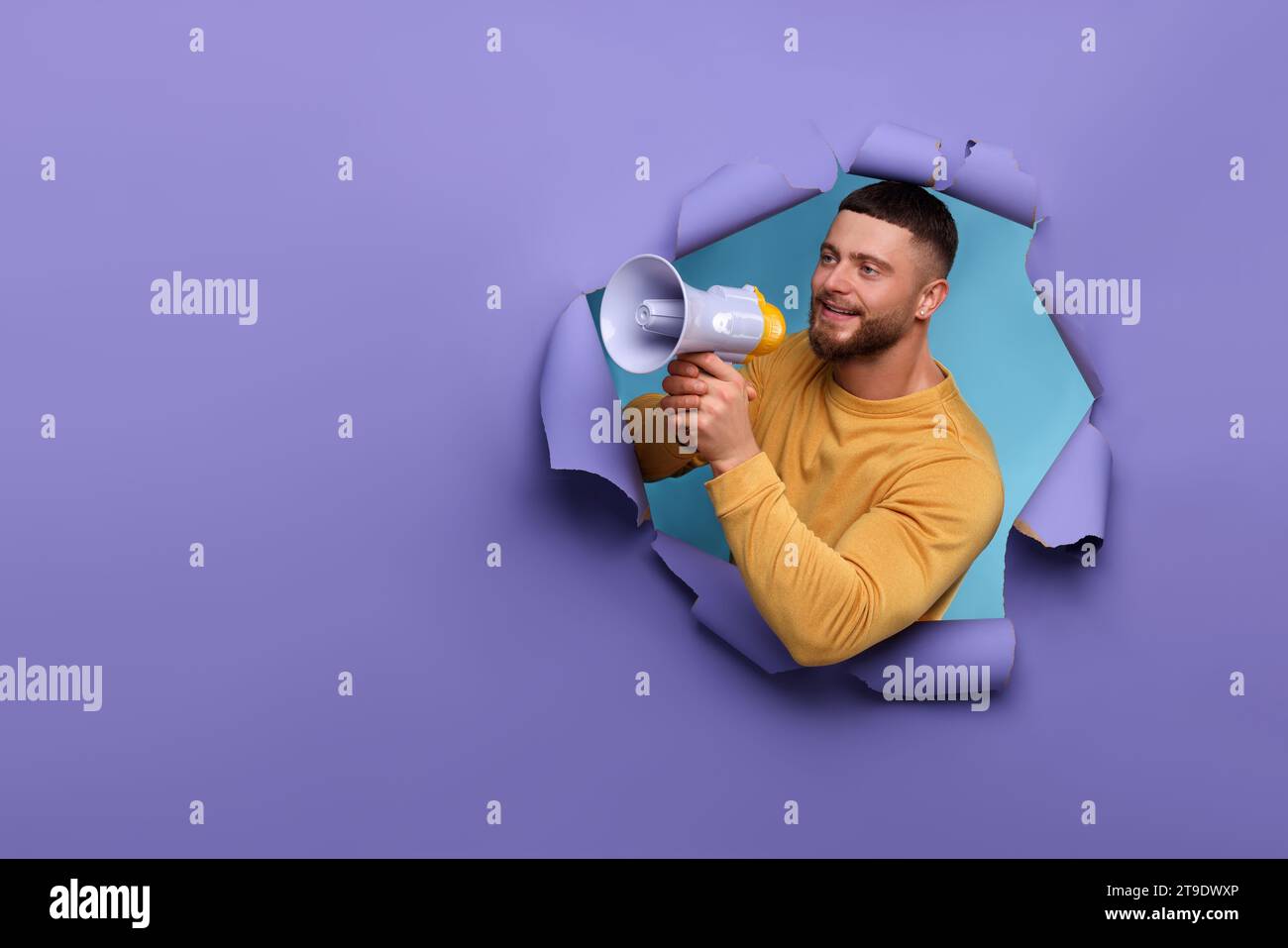 Special promotion. Young man with megaphone shouting through hole in ...