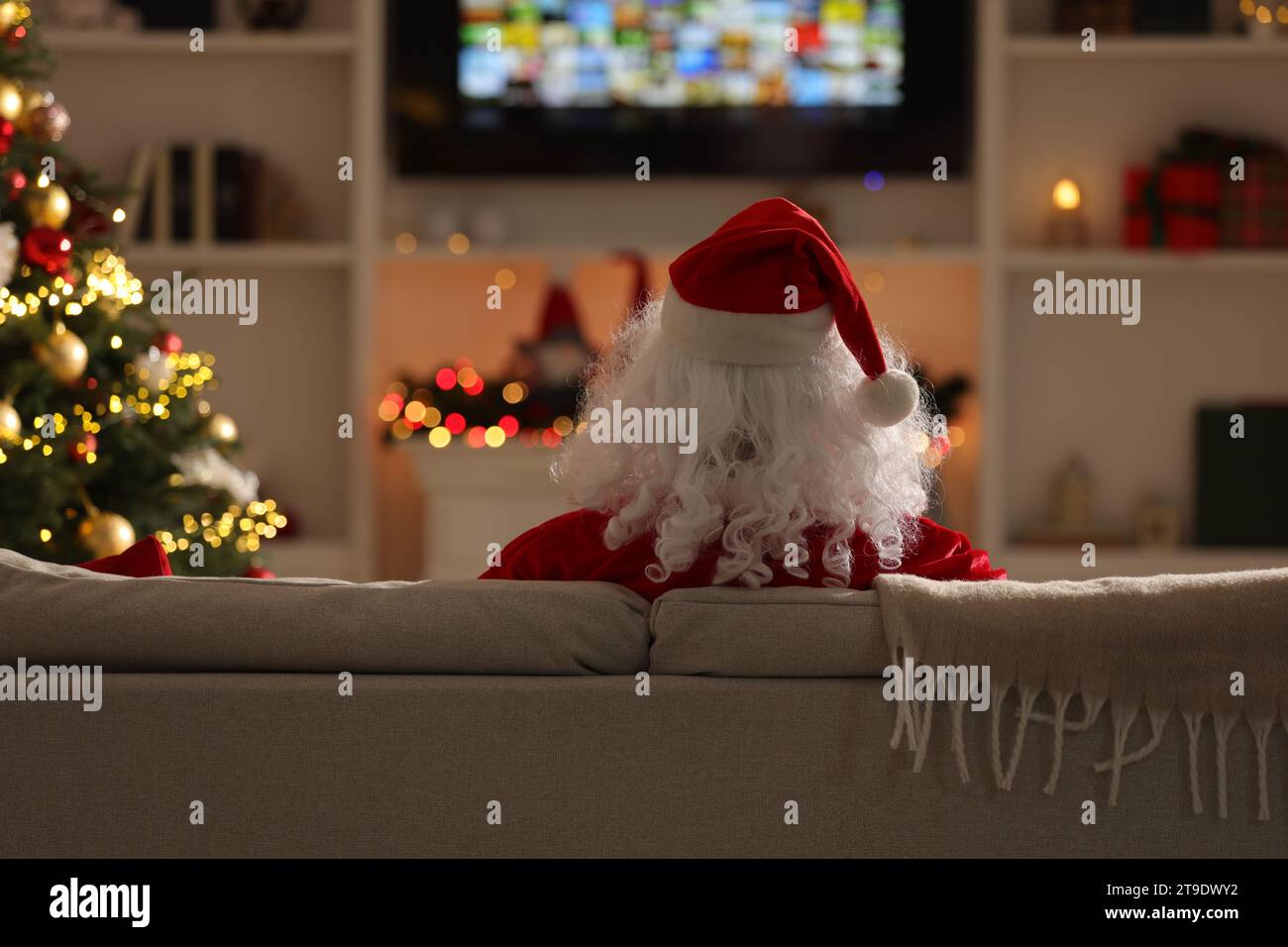 Merry Christmas. Santa Claus watching TV on sofa at home, back view ...