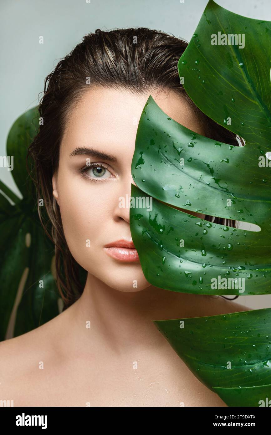 Portrait of beautiful young woman with a smooth skin holding Monstera ...