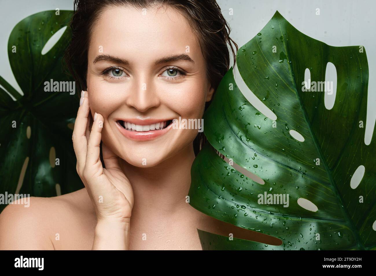 Portrait of beautiful young woman with a smooth skin holding Monstera ...