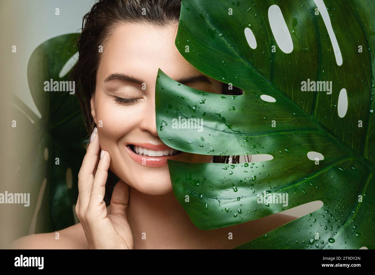 Portrait of beautiful young woman with a smooth skin holding Monstera ...