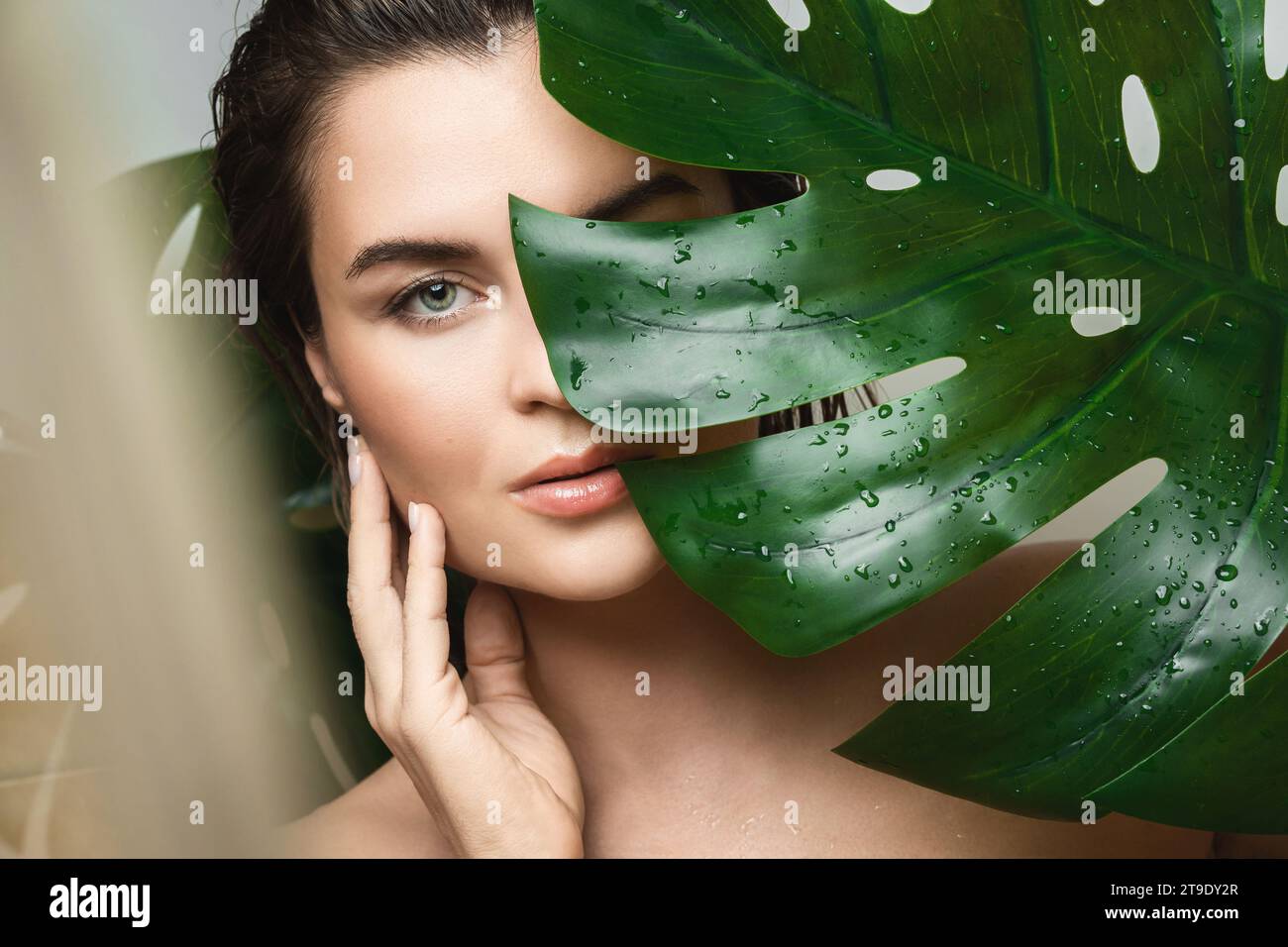 Portrait of beautiful young woman with a smooth skin holding Monstera ...