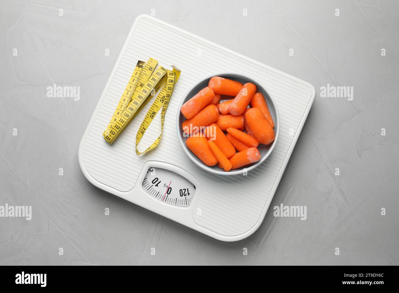Healthy diet. Scale with carrots and measuring tape on light grey table ...