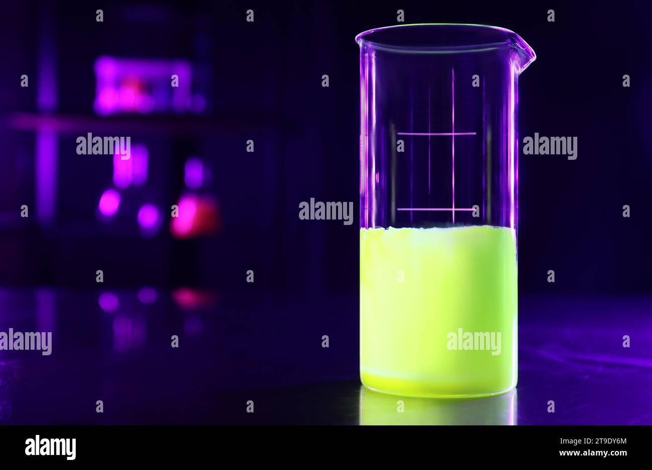 Laboratory beaker with luminous liquid on table against dark background ...
