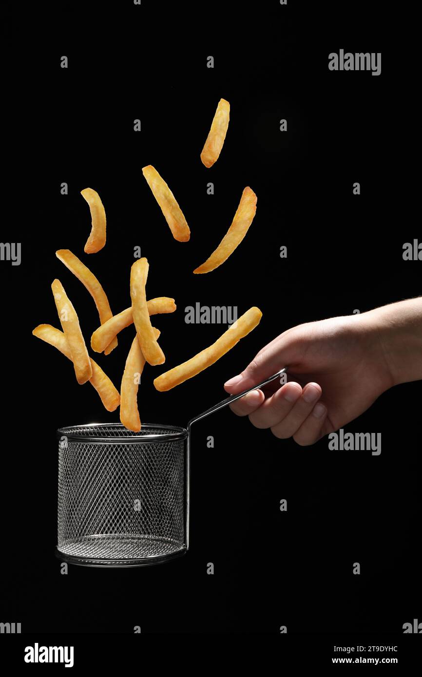 French fries falling into metal basket held by woman on black ...