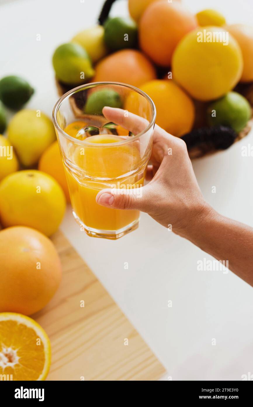 Closeup of female hand with a glass of freshly squeezed orange juice ...