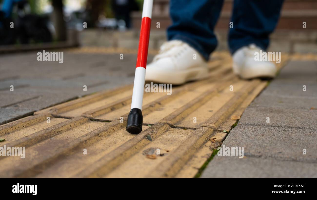 A blind woman walks on the street on tactile yellow tiles. Focus on the ...