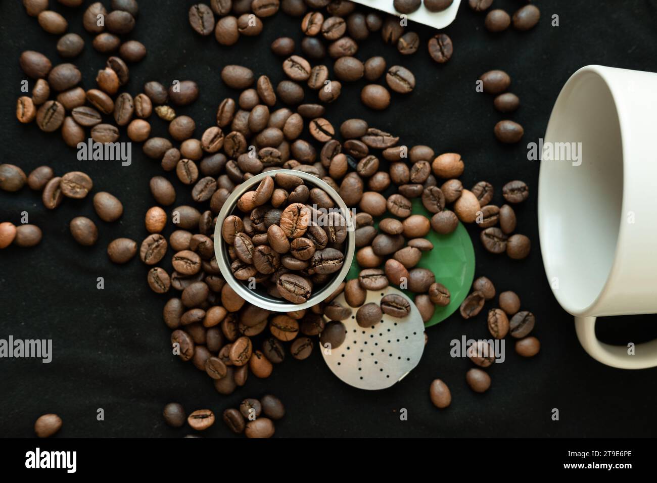 Coffee beans inside and around a refillable coffee capsule on a black ...