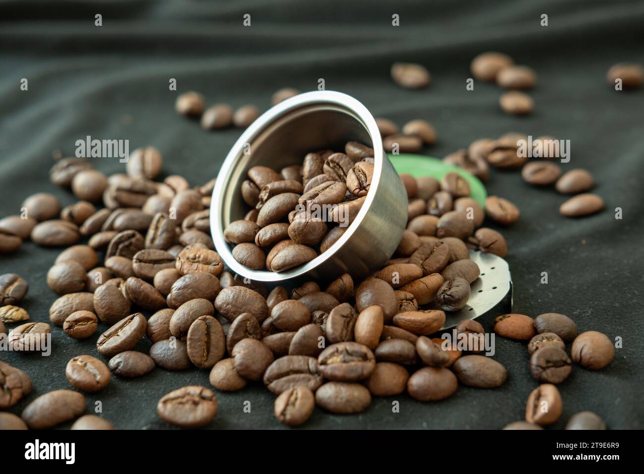 Coffee beans inside and around a refillable coffee capsule on a black ...