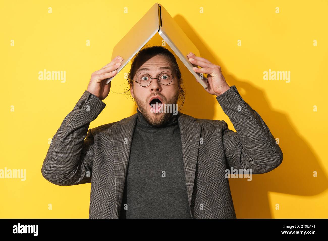 Shocked bearded man holding laptop computer above his head on yellow ...