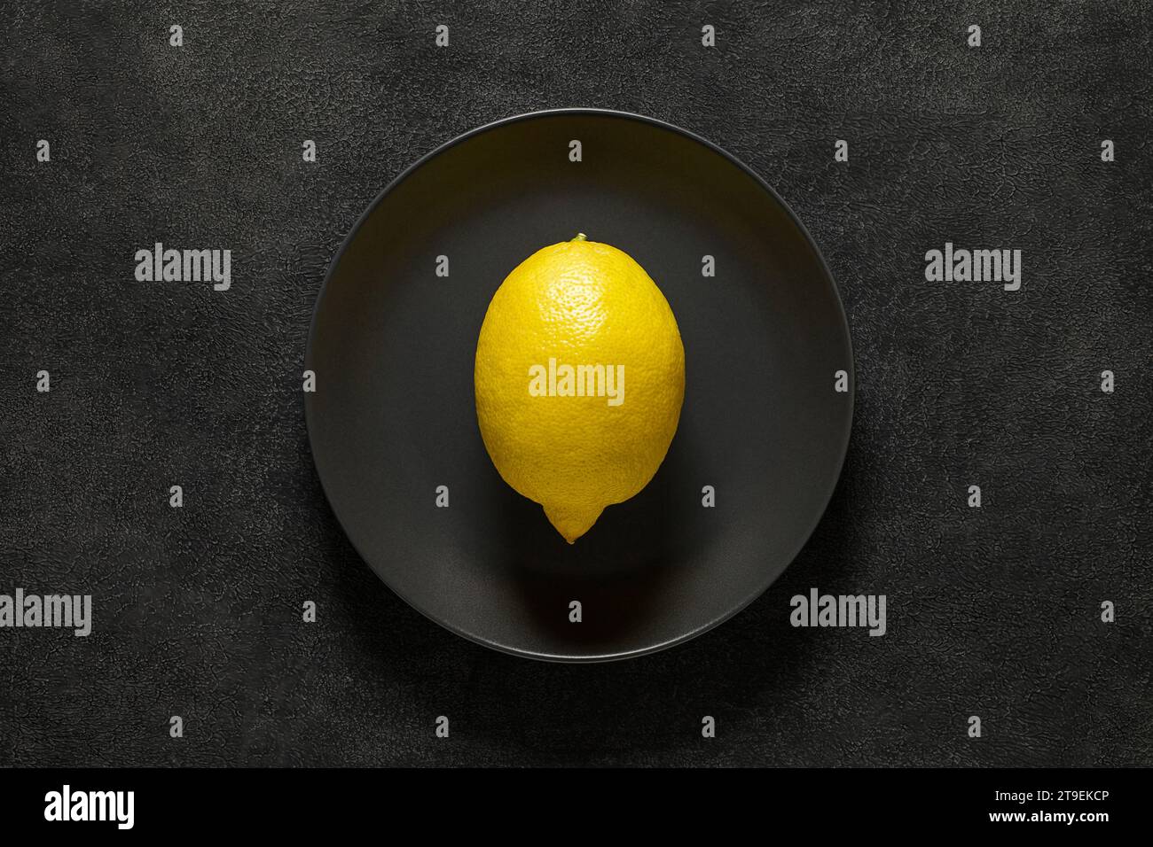 One whole lemon on grey plate, on dark background, top view, space to ...