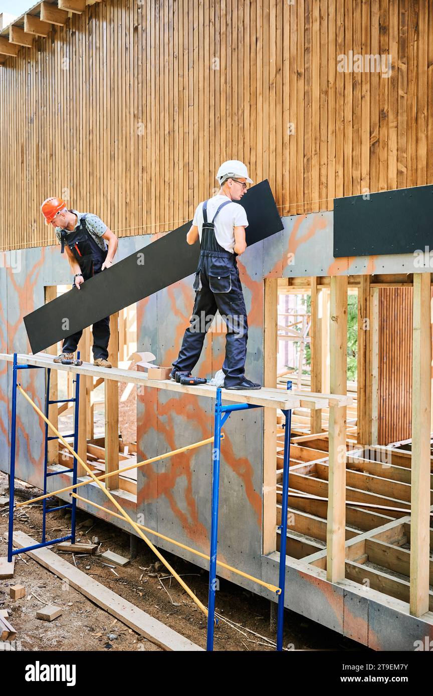 Carpenters constructing wooden framed house. Two men workers cladding ...