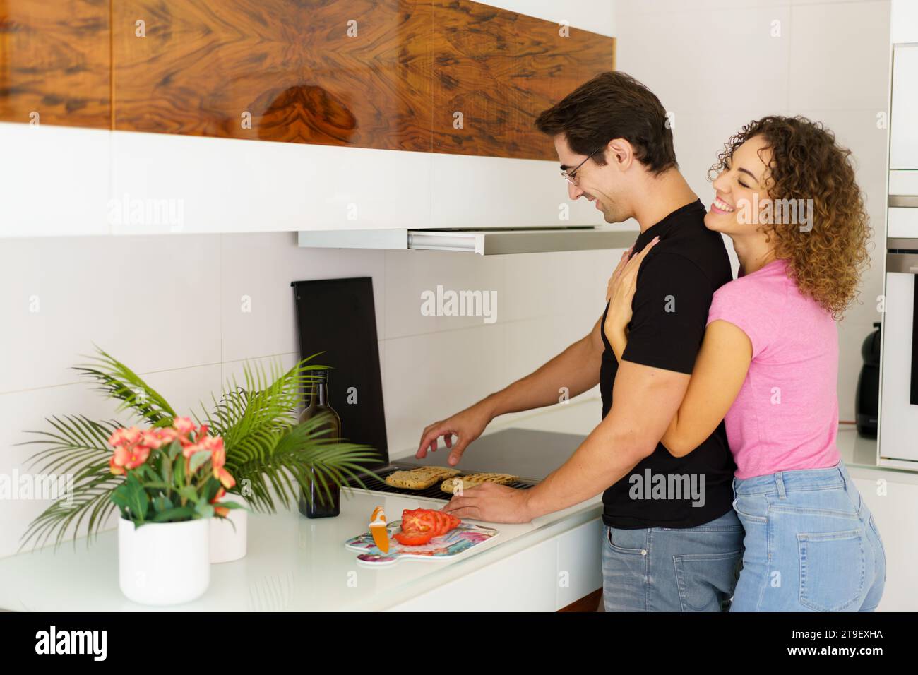 Side view of happy adult couple while standing near cooking range ...