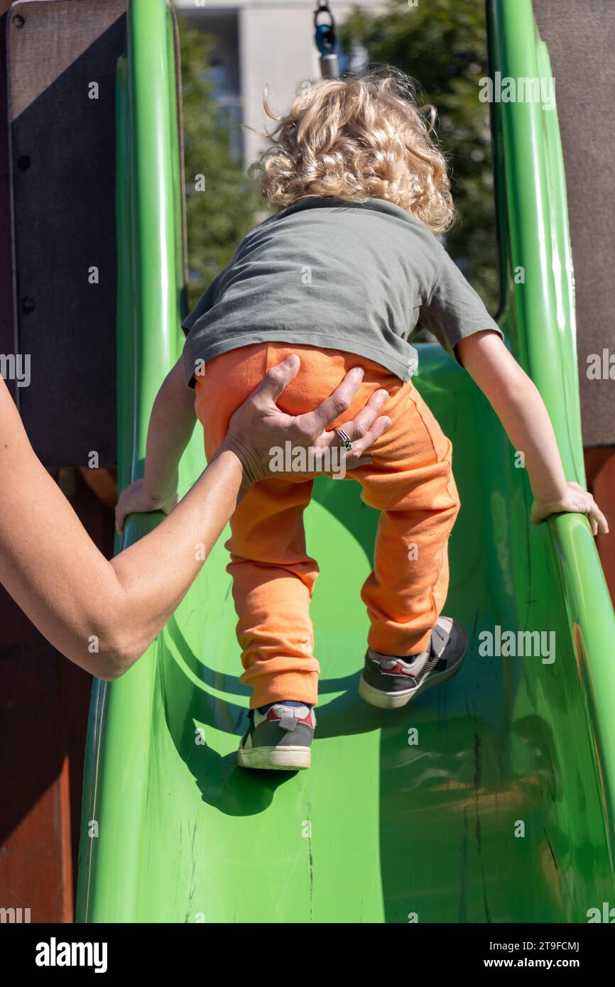 A little boy climbs the slide with the help of his mother Stock Photo ...