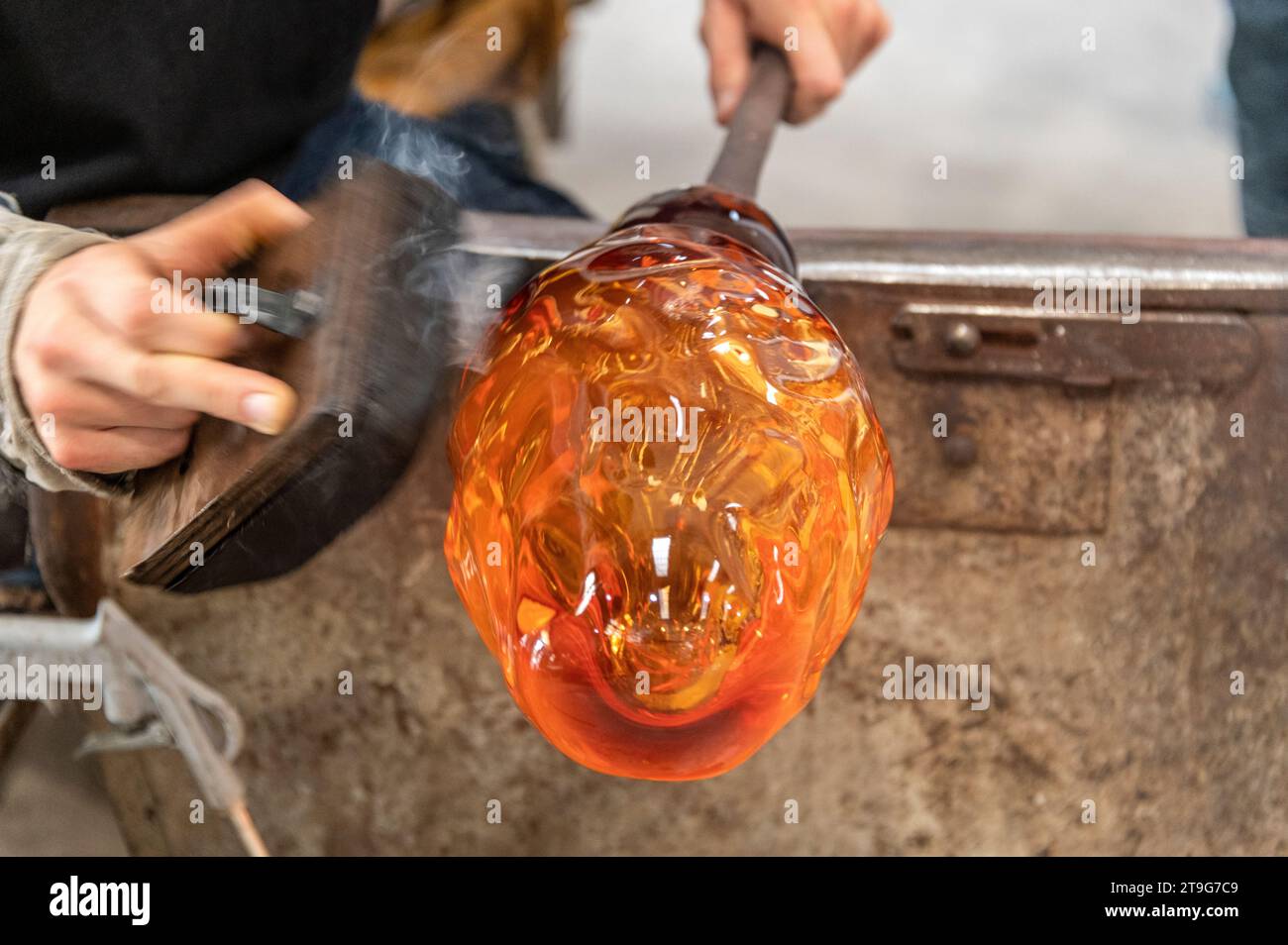 A glassblower skilfully shapes a heated molten mould of clear glass ...