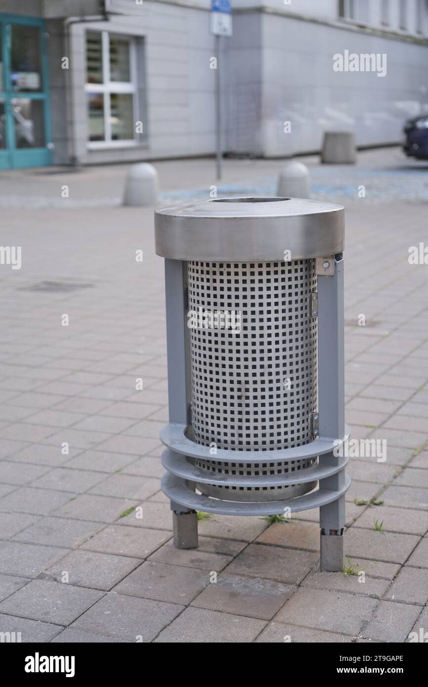 Single modern metal trash bin on a concrete sidewalk with a light grey ...