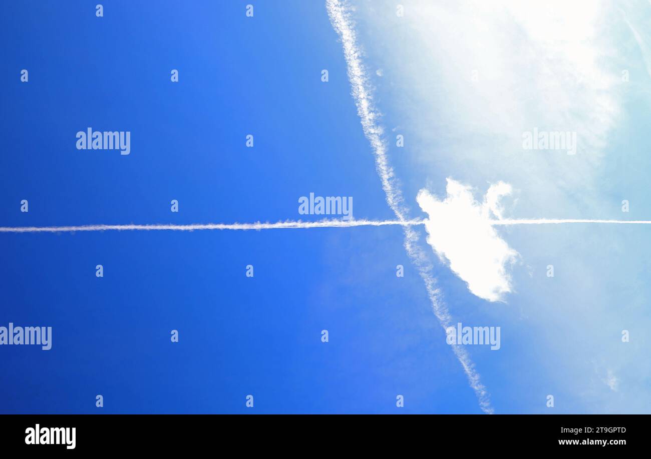 long white trails high in the blue sky crossing a cloud without ...