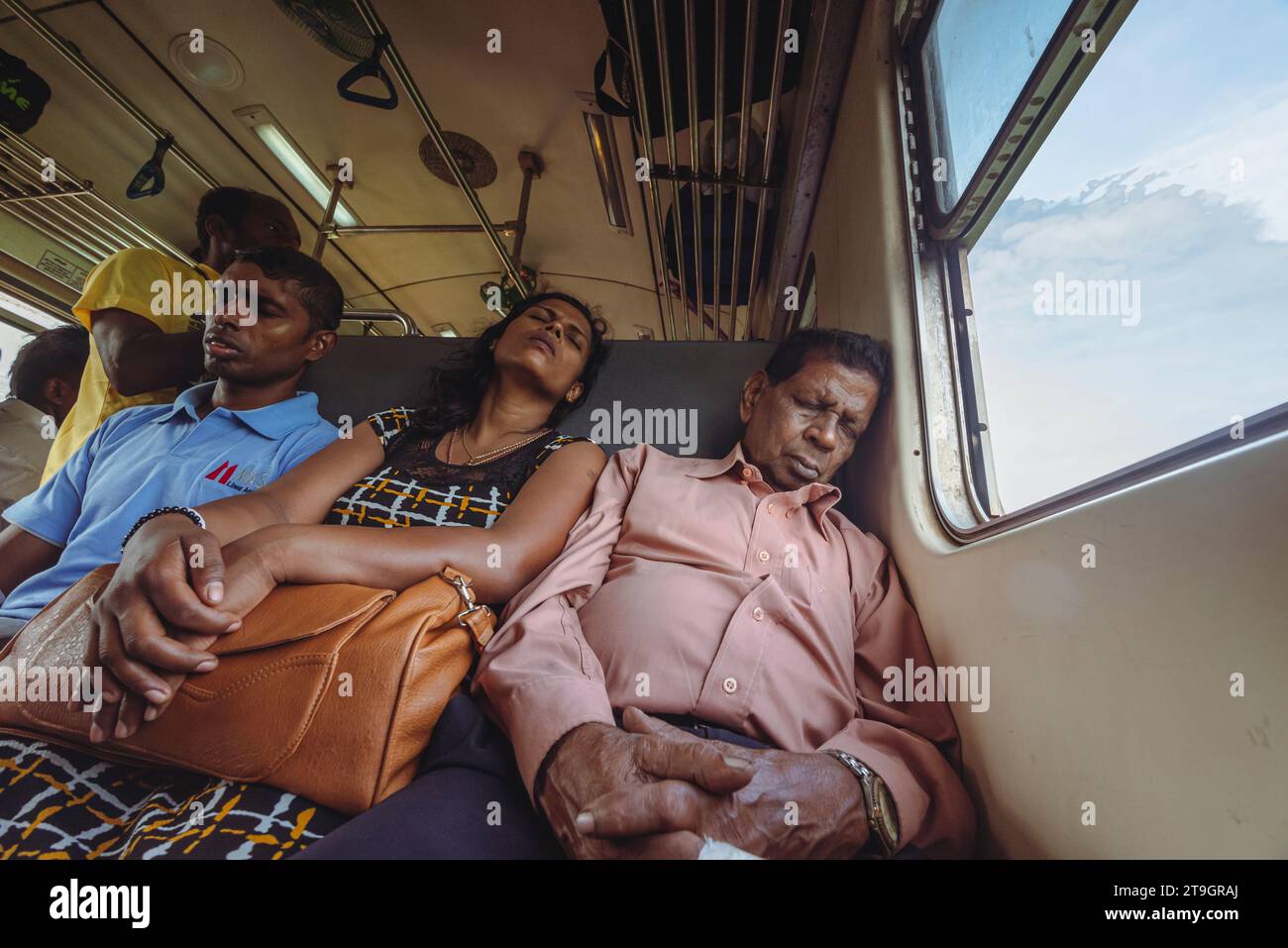 Three people sleep on a bench seat on a train from Colombo in Sri Lanka ...