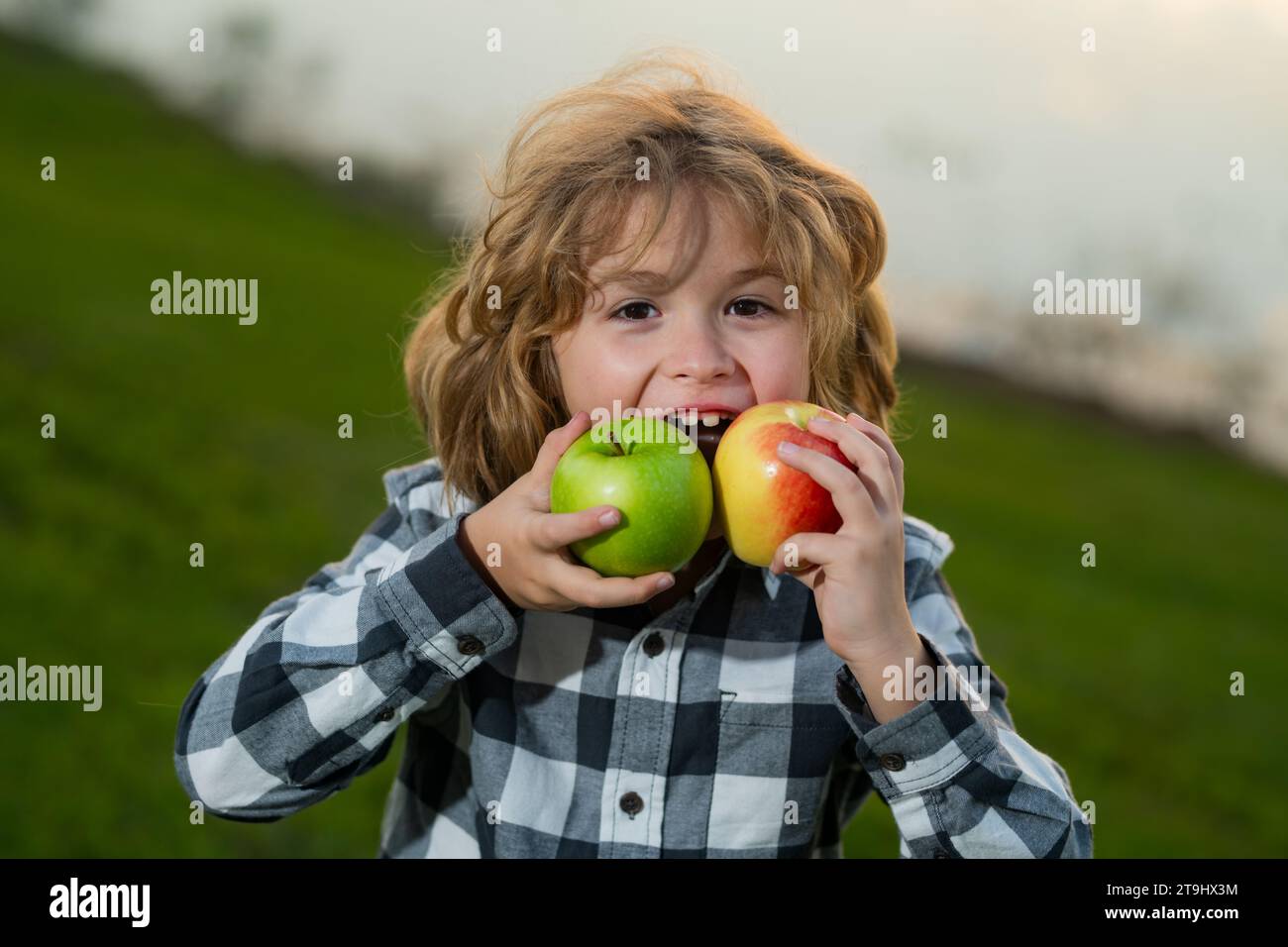 Kid dressed casual holding and apple with a smile and showing eats ...