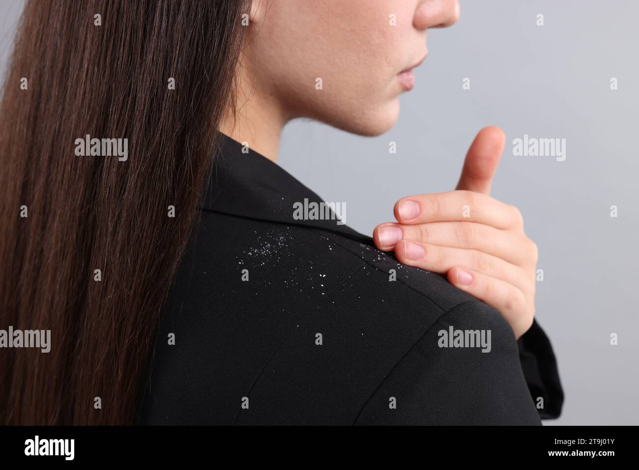 Woman brushing dandruff off her jacket against light grey background ...