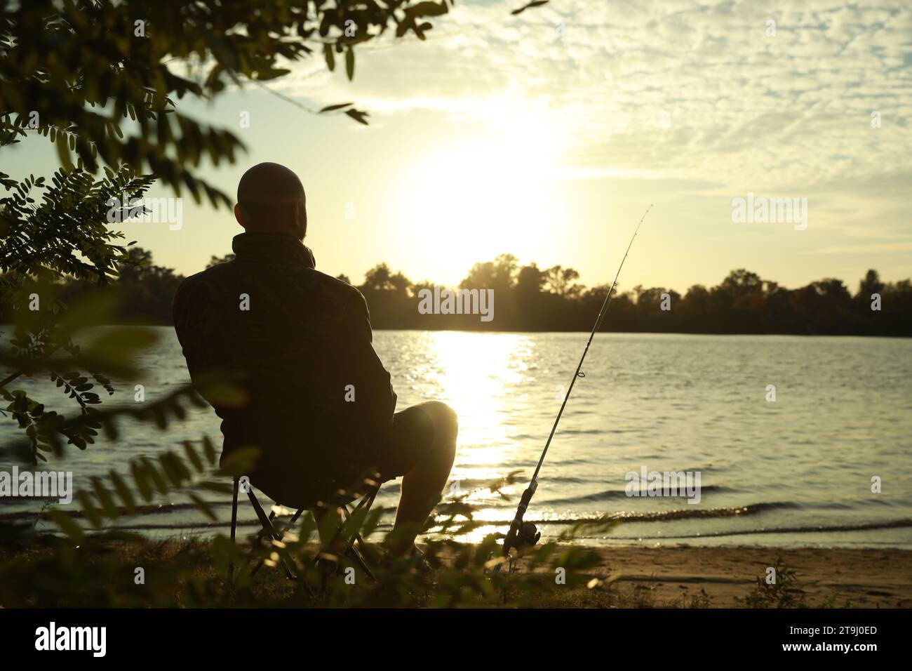 Fisherman with rod sitting on folding chair and fishing at riverside ...