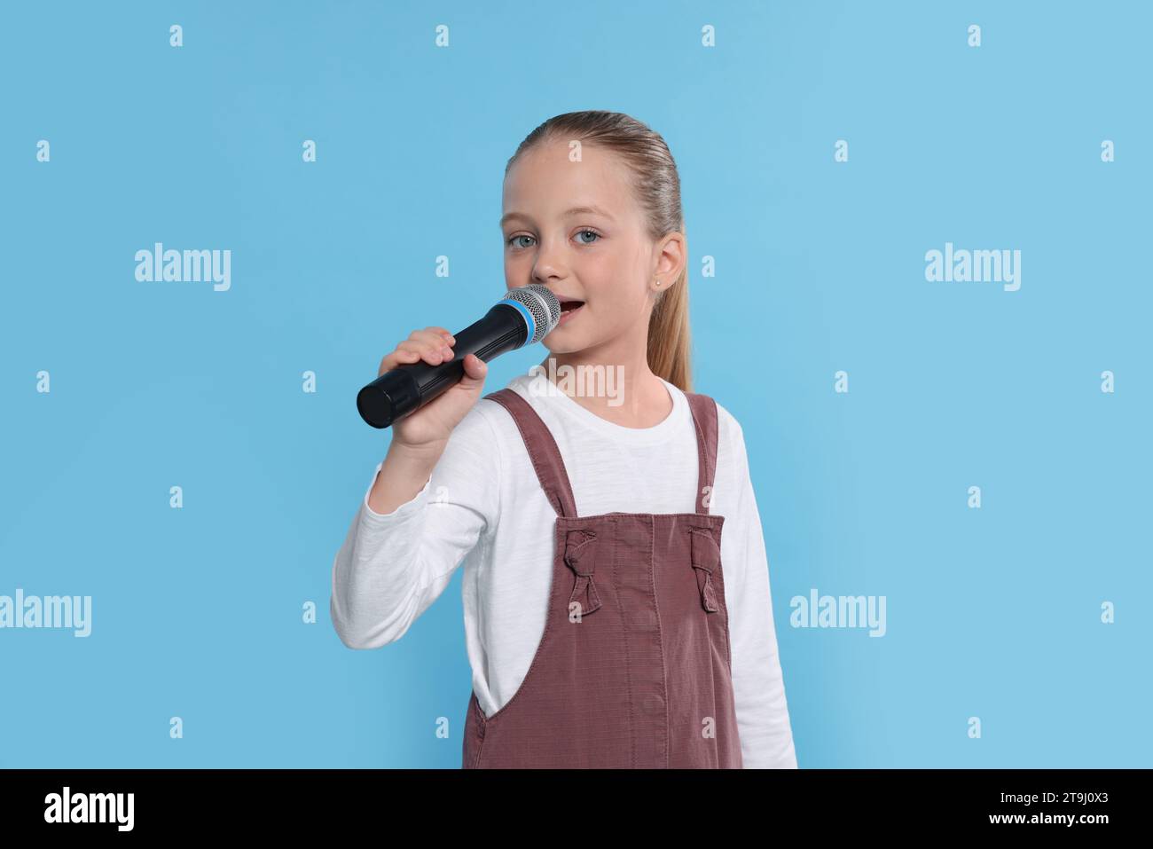 Cute little girl with microphone singing on light blue background Stock ...