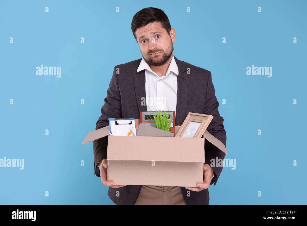 Unemployed man with box of personal office belongings on light blue ...