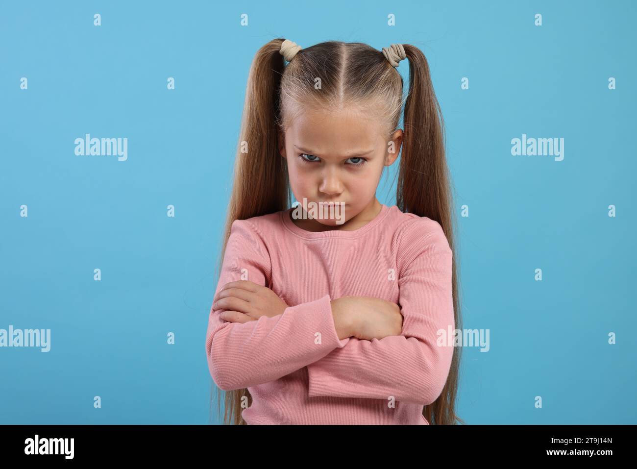 Resentful girl with crossed arms on light blue background Stock Photo ...