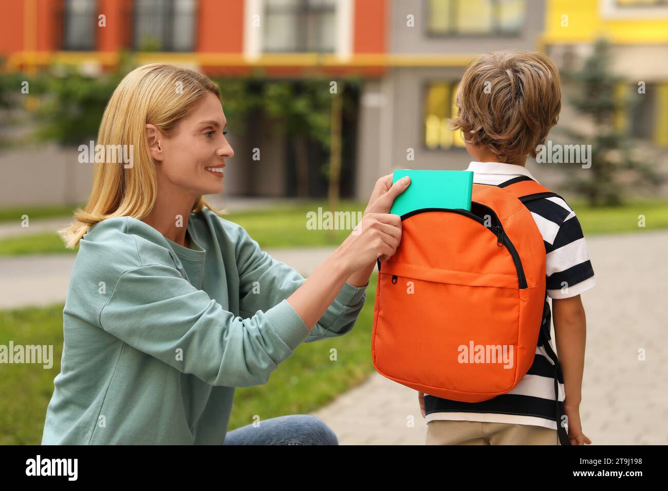 Happy woman putting notebook into with her son's backpack near ...
