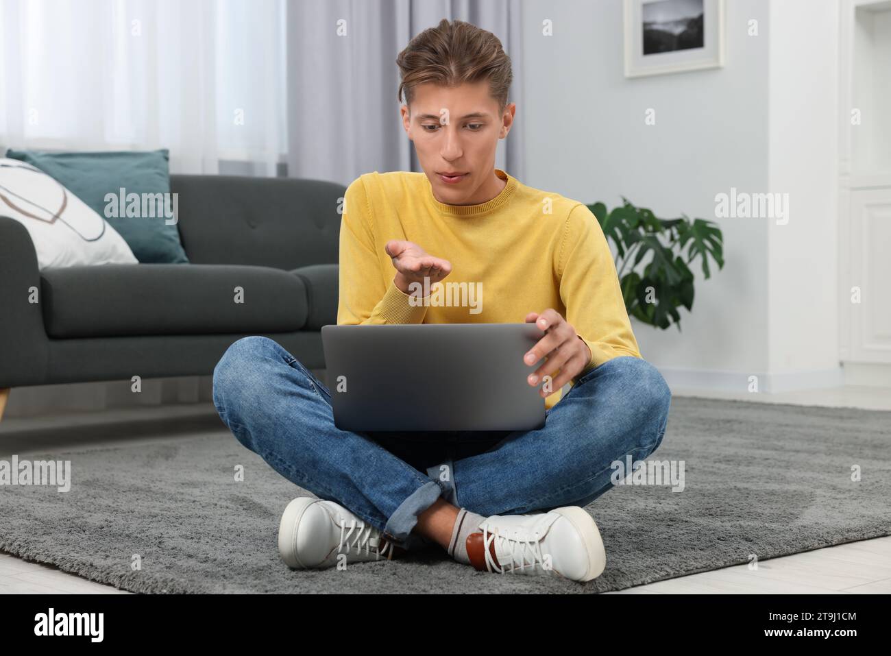 Happy young man having video chat via laptop and blowing kiss on carpet ...