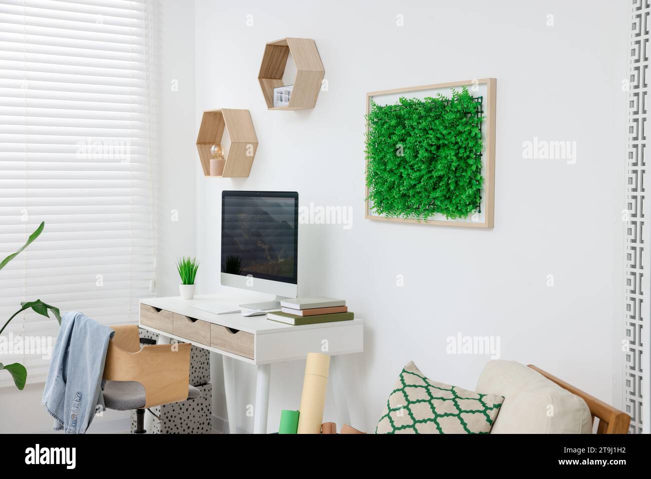 Green artificial plant wall panel and desk with computer in light room ...