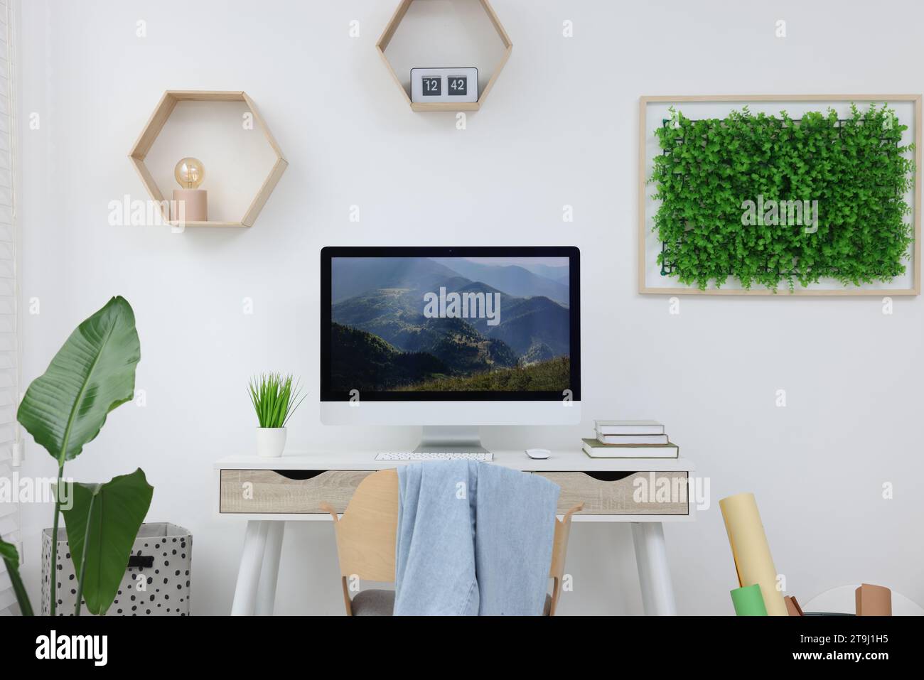 Green artificial plant wall panel and desk with computer in light room ...